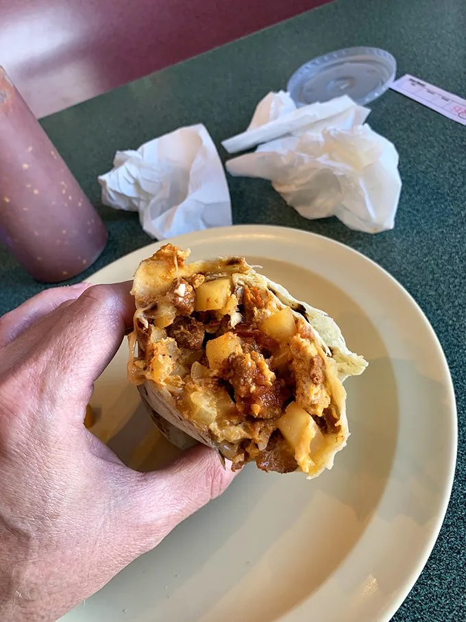 That sandwich in the background is merely a spectator to the real star – a burrito so gloriously smothered it requires strategic planning before the first bite.