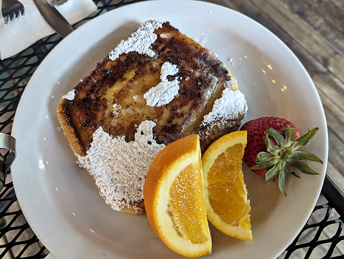 French toast dusted with powdered sugar, flanked by fresh fruit—breakfast that straddles the line between meal and dessert with delicious defiance.
