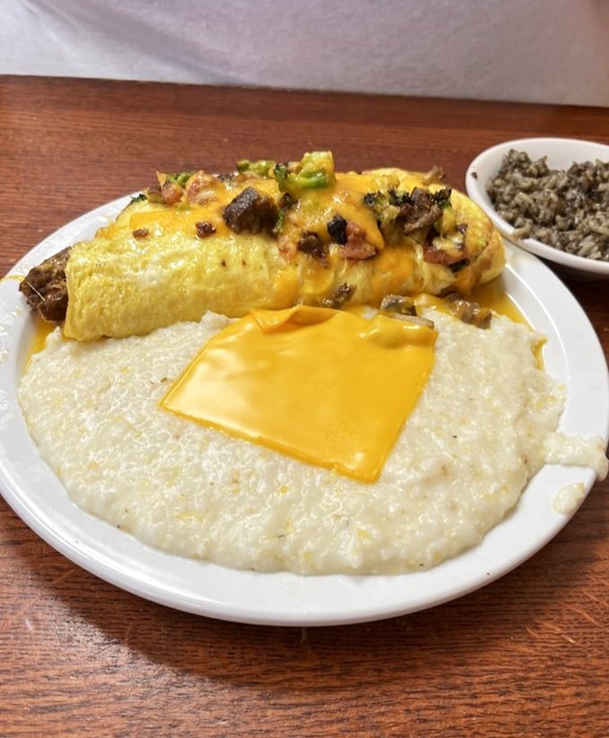 This omelet doesn't just sit on the plate—it commands attention. Melted cheese cascades over fluffy eggs while grits stand by, ready for their moment.
