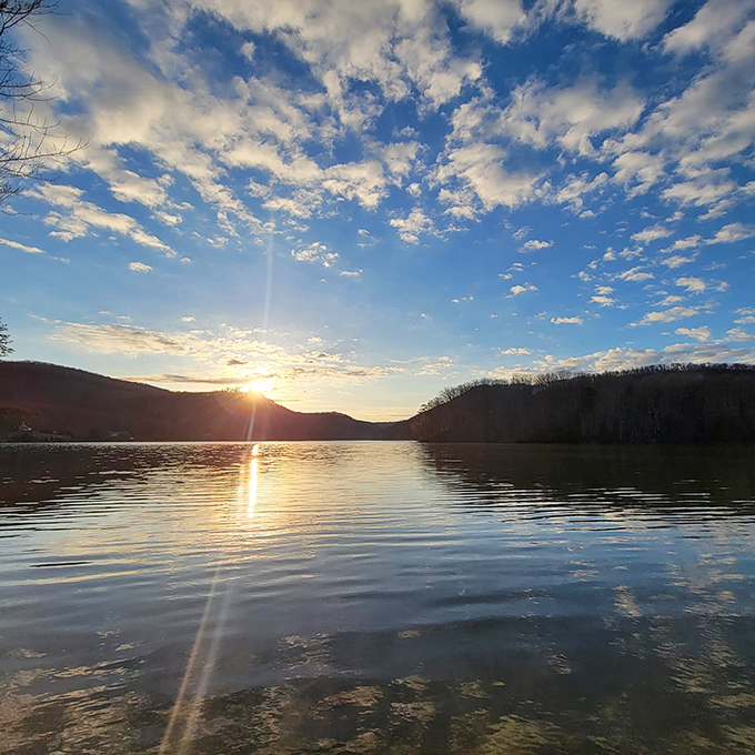 Nature puts on its nightly watercolor show as sunset paints the Kentucky sky, reflecting golden hues across still waters that mirror the surrounding hills.