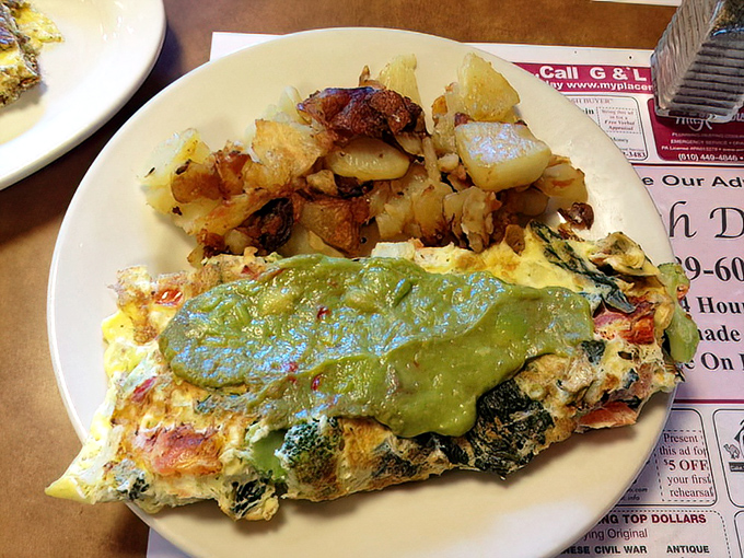 Green goddess meets morning masterpiece—this veggie omelet wears its avocado crown proudly while potatoes huddle nearby, crisped to golden perfection. 