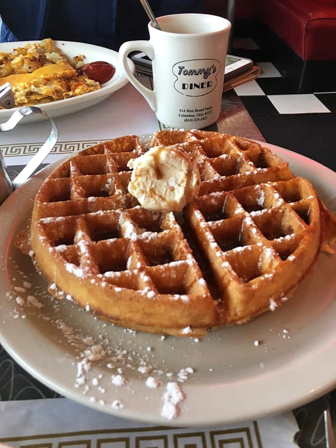 A waffle that understands its purpose in life – golden, crisp-edged perfection dusted with powdered sugar and crowned with a melting butter hat.