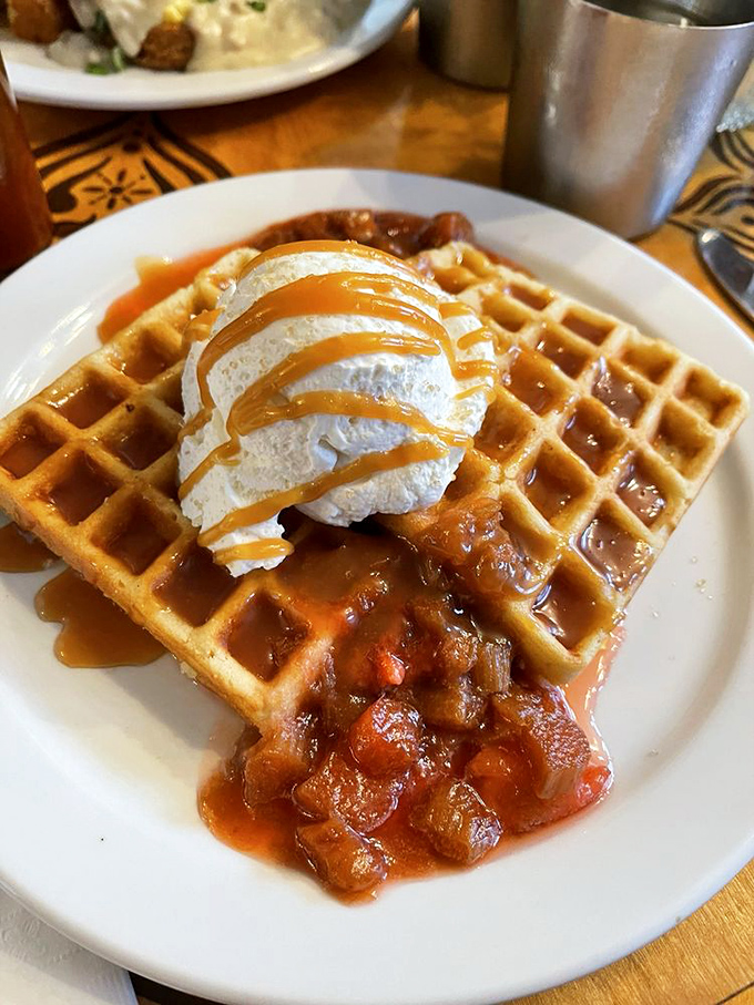 Waffle architecture at its finest—golden foundation, strawberry-rhubarb compote middle layer, whipped cream penthouse, and a caramel drizzle that defies gravity.