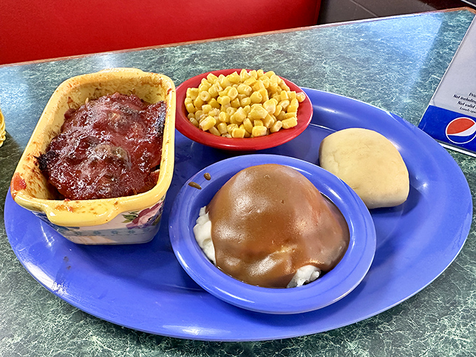 Meatloaf, mashed potatoes smothered in gravy, corn, and a roll—the Mount Rushmore of comfort food carved onto a single blue plate.