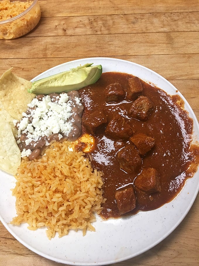 A plate that proves heaven exists on earth. Rice, beans, and chile colorado—the holy trinity of comfort that makes you want to hug the chef.