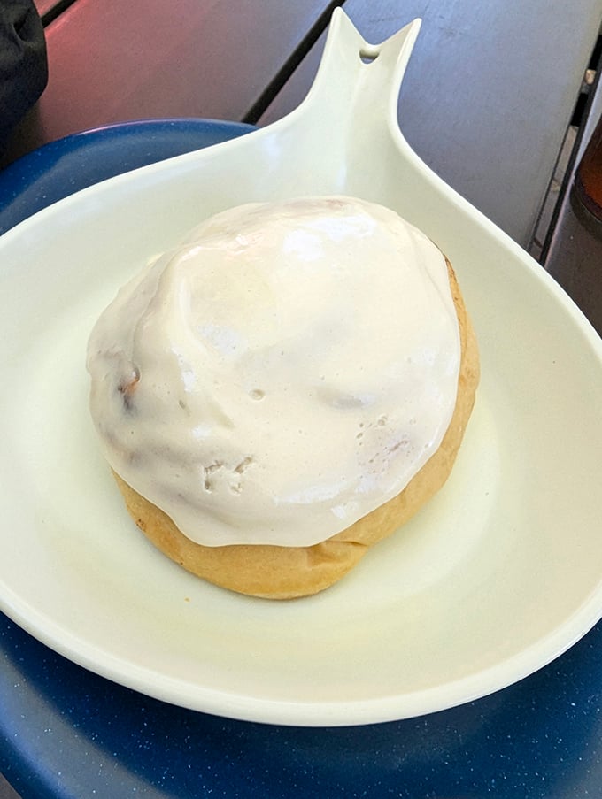 This isn't just a cinnamon roll—it's a pillowy spiral of morning bliss wearing a generous coat of cream cheese icing that melts into every nook.