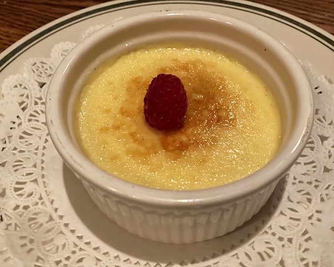 Crème brûlée with a crust that cracks like thin ice on a perfect winter morning. That lone raspberry is the cherry on top—except it's a raspberry.