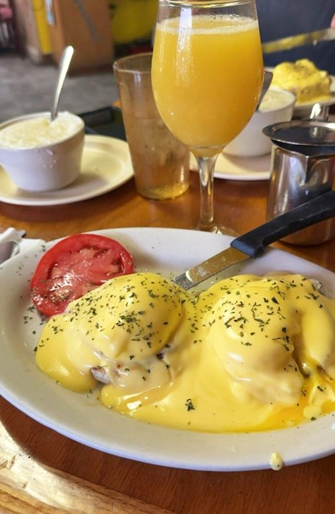 Eggs Benedict with a Florida twist – sunshine-yellow hollandaise cascading over poached eggs like a breakfast waterfall, with a splash of orange juice to complete the morning.