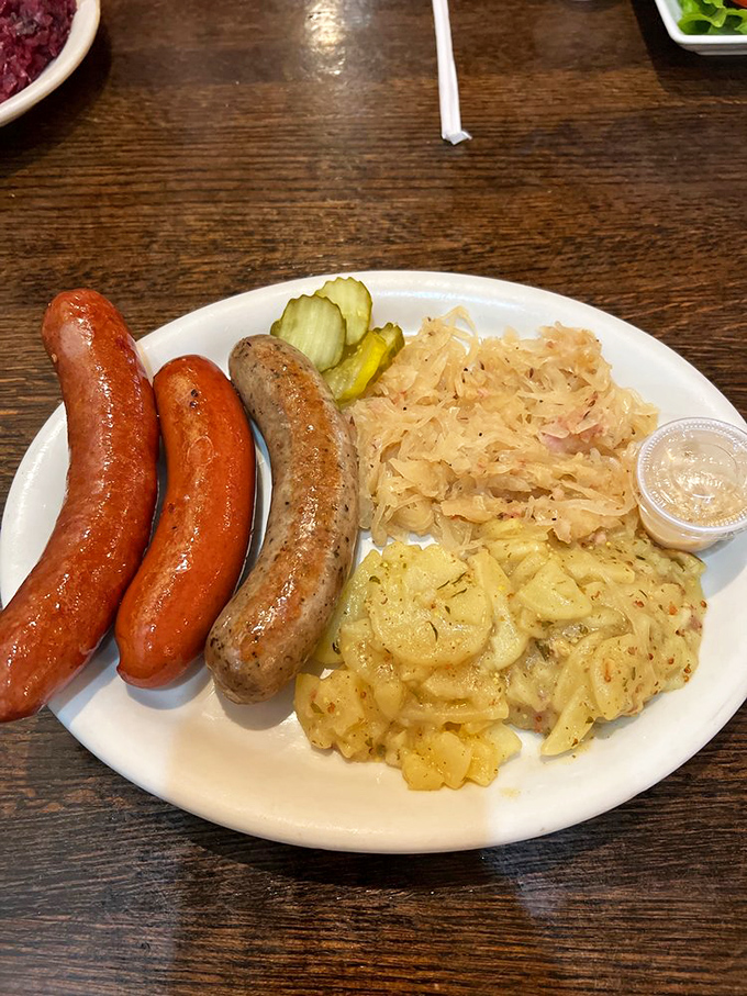 A sausage trio that would make any Bavarian proud, nestled alongside tangy sauerkraut and German potato salad – comfort food with a passport.