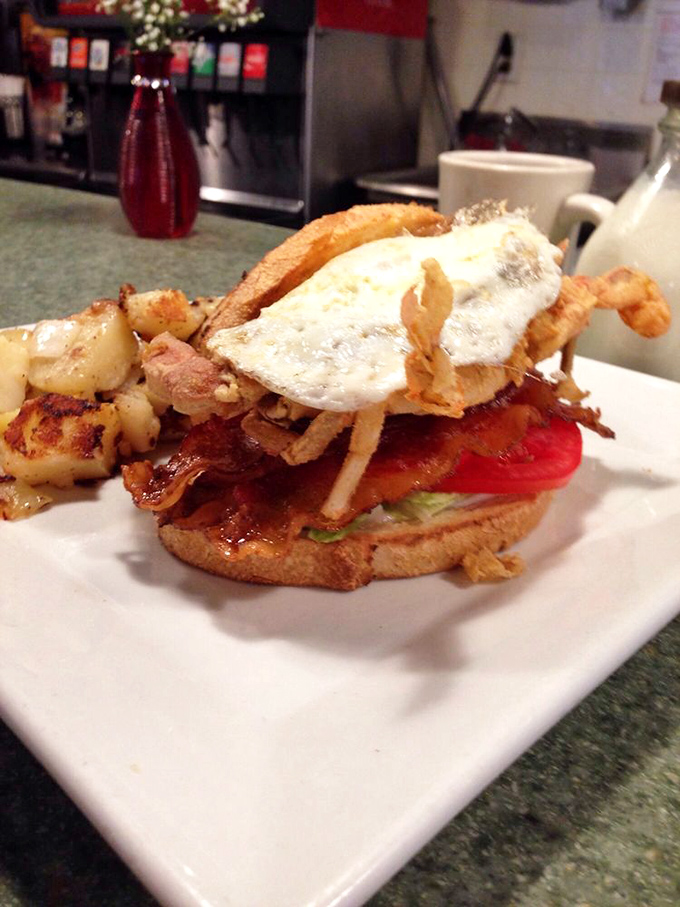The architectural marvel that is this sandwich—crispy bacon, fresh tomato, and what appears to be soft-shell crab, all crowned with a perfectly fried egg.