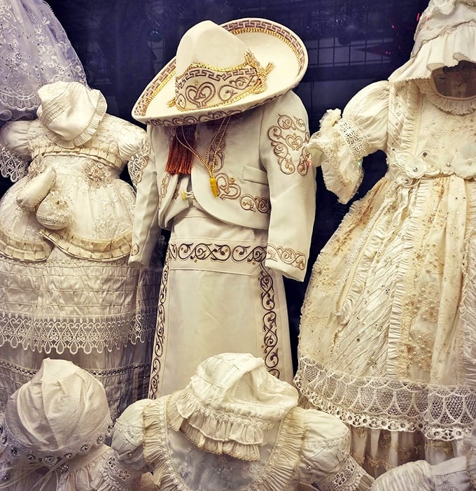 Baptism gowns and charro suits hang in pristine white splendor—ceremonial garments that transform ordinary moments into memories that last generations.