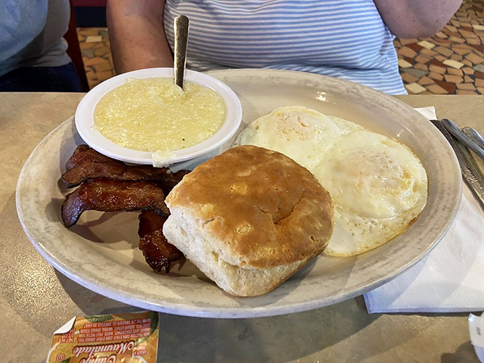 Breakfast simplicity perfected: eggs, bacon, grits, and a biscuit that could make a carb-counter weep with joy and regret simultaneously.