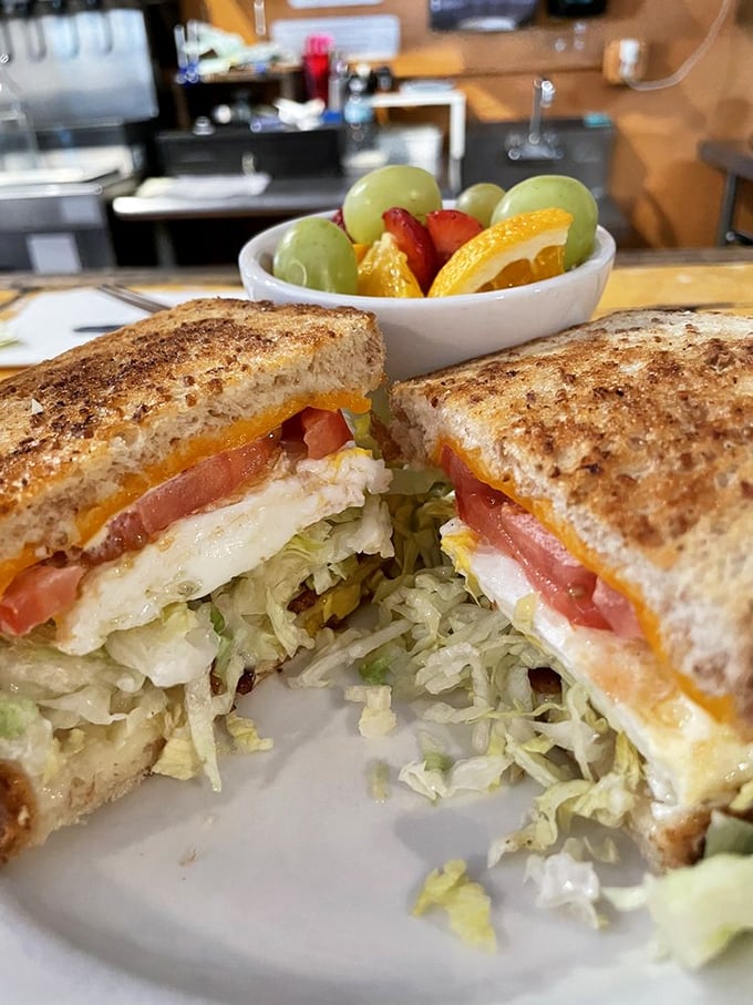 This breakfast sandwich isn't just stacked—it's architecturally sound. Fresh veggies, melted cheese, and eggs between perfectly toasted bread with fruit playing supporting roles.