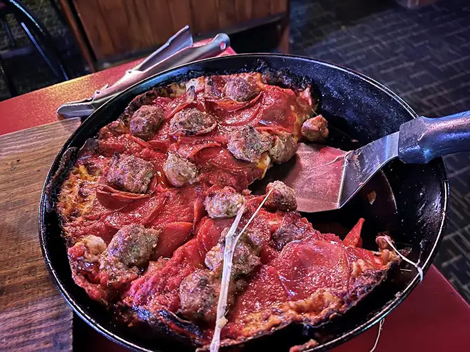 The spatula reveals the masterpiece beneath—a sausage and pepperoni deep dish with that coveted caramelized cheese edge. Pizza dreams are made of this.