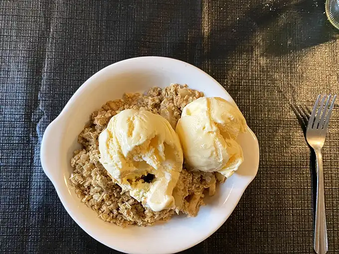 Apple crisp crowned with vanilla ice cream—the dessert equivalent of a warm hug from your favorite grandparent after a satisfying meal.