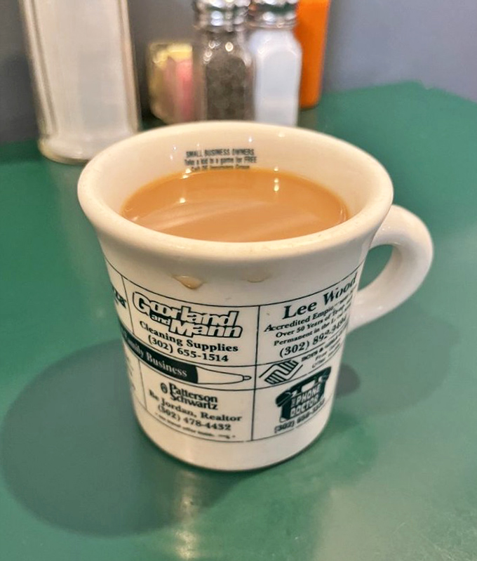 That perfect diner coffee—not fancy, not pretentious, just reliable as sunrise and served in a mug advertising local businesses.
