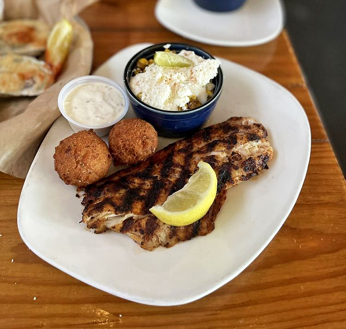 A plate where land meets sea—grilled fish resting beside hushpuppies and street corn that's dressed up enough for a night on the town.