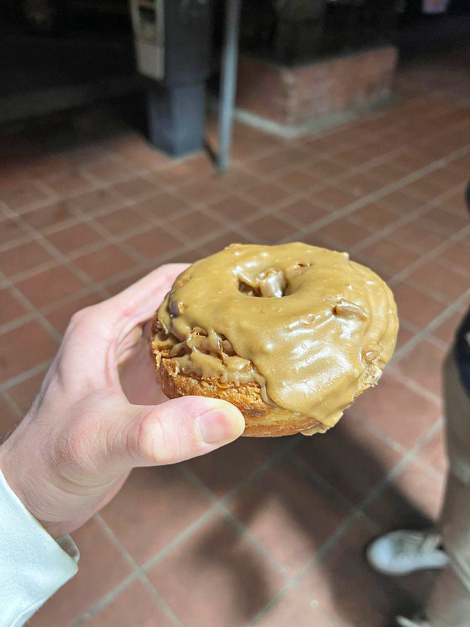 Someone's holding happiness in their hand—a perfectly glazed maple donut that's about to make their day approximately 300% better.