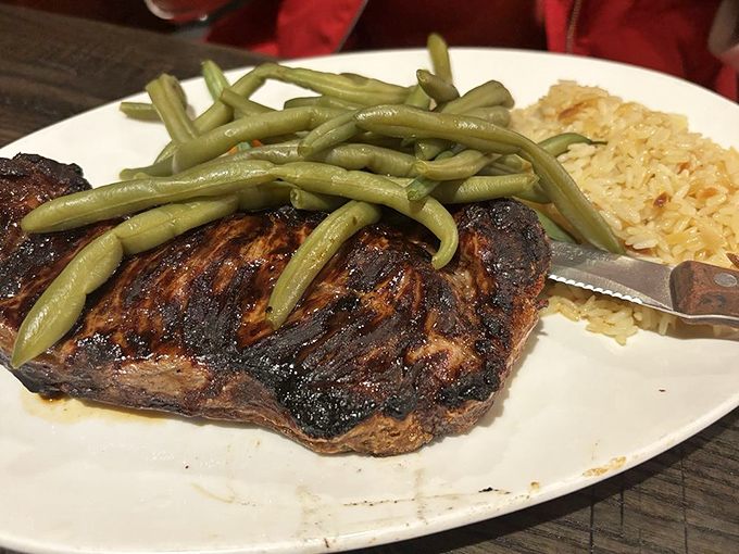 A perfectly grilled steak topped with green beans and rice pilaf—the kind of straightforward, honest plate that makes you wonder why anyone bothers with fancy restaurants.