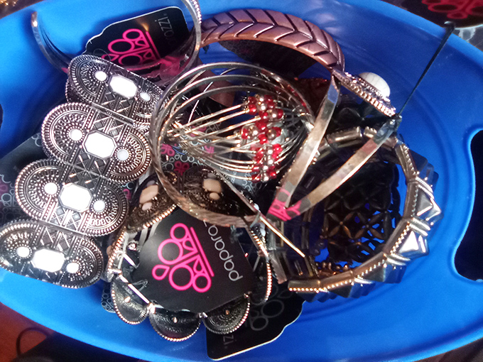 A blue bin of jewelry treasures where vintage brooches and contemporary pieces mingle like guests at an eclectic cocktail party.
