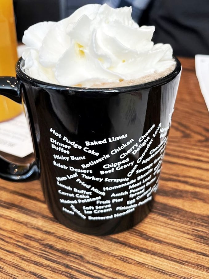 Hot chocolate topped with a cloud of whipped cream so generous it deserves its own zip code. The mug lists menu items like a delicious treasure map.