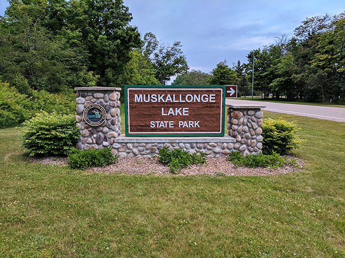 The welcoming sign at Muskallonge Lake State Park promises adventures between two bodies of water—like getting a two-for-one deal on nature.