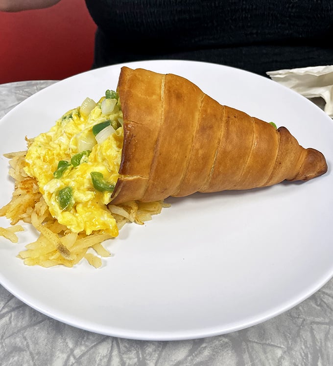 A croissant breakfast sandwich reinvented as edible architecture – eggs and veggies nestled in golden-brown pastry with hash browns standing guard.