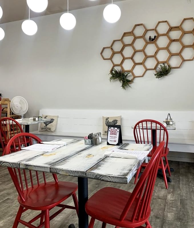 Red Windsor chairs pop against whitewashed tables beneath a honeycomb wall display – farmhouse chic that doesn't try too hard.