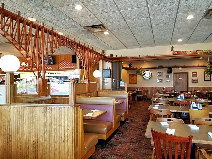 The wooden trestle bridge spanning the dining room isn't just decor—it's functional art, carrying miniature trains above conversations and comfort food below.