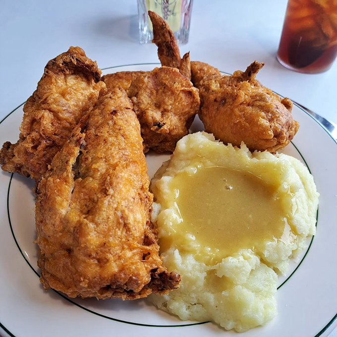 Fried chicken with a crust that shatters like glass, alongside mashed potatoes cradling a golden pool of gravy. Comfort food that actually comforts.