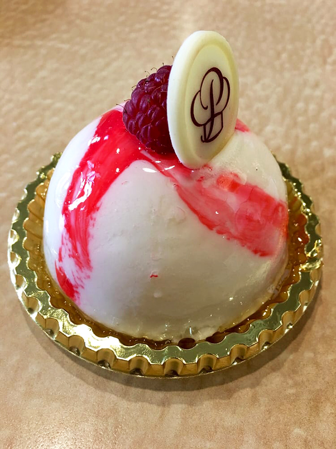 This dome-shaped masterpiece isn't just dessert—it's architecture. The raspberry and white chocolate glaze create edible modern art on a gold pedestal.