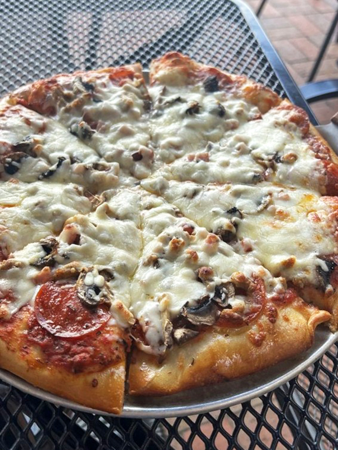 The holy trinity of pizza toppings – pepperoni, mushroom, and sausage – nestled under a blanket of cheese that stretches like your favorite sweater.