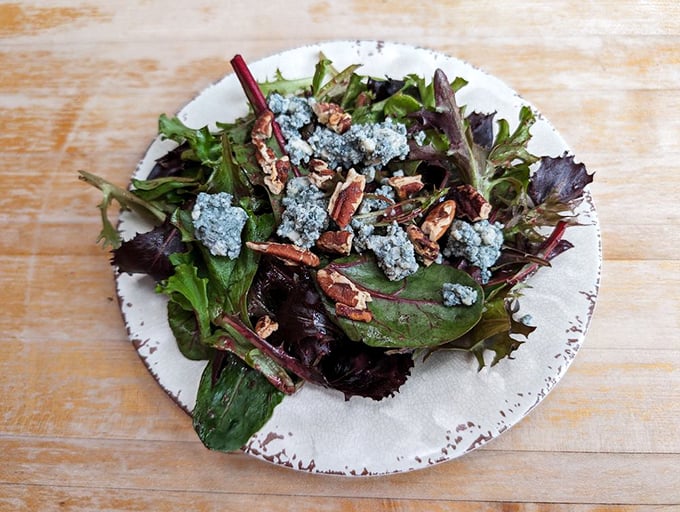 Even the side salad deserves attention here—fresh greens, blue cheese crumbles, and pecans create a symphony of textures and flavors.