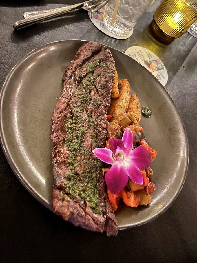 This skirt steak wearing its chimichurri crown sits majestically beside roasted vegetables. The orchid isn't just garnish—it's applauding the chef's achievement.