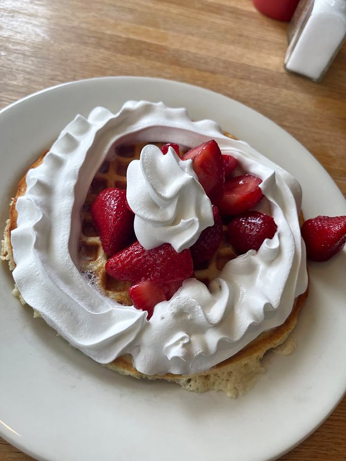 A waffle wearing whipped cream like a cloud collar, with strawberries playing the role of rubies. Breakfast or dessert? Yes.