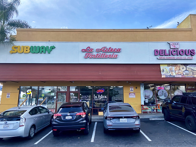 The vibrant red and yellow façade of La Azteca Tortilleria stands like a beacon of culinary promise on Cesar Chavez Avenue.