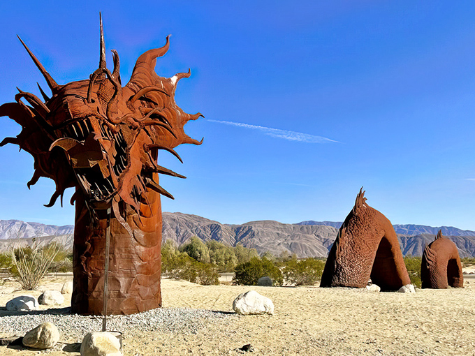 The dragon emerges from desert sands like a rusty leviathan, its metallic scales catching California sunlight while mountains stand guard in the distance.