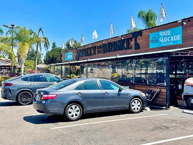 The wooden facade of Smokey and The Brisket stands like a barbecue beacon under the California sun, palm trees swaying as if drawn by the smoky aroma.
