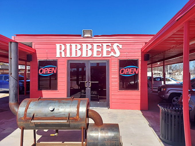 The bright red exterior of Ribbee's isn't subtle – it's like Texas itself, boldly announcing "serious barbecue happens here" with its weathered smoker standing guard.