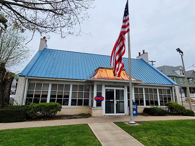 That iconic blue roof signals breakfast paradise like a beacon to hungry travelers. The American flag proudly announces: "Real diner food served here!"