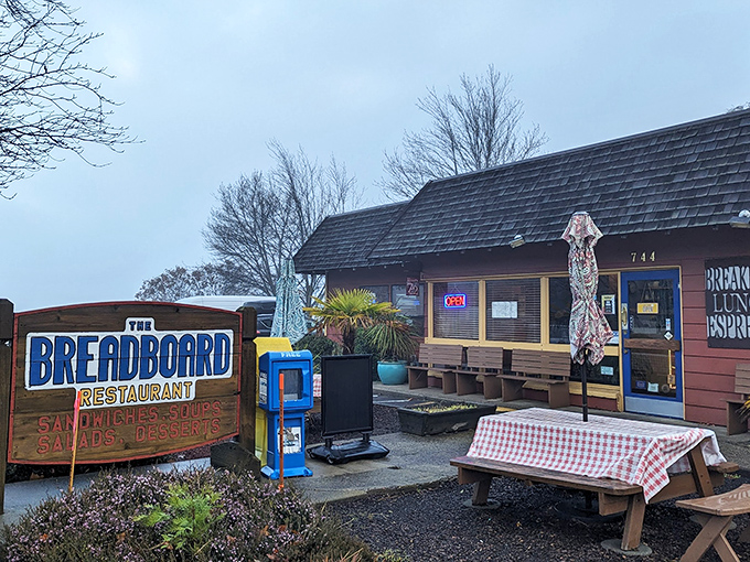 The rustic cabin exterior of The Breadboard promises comfort food nirvana. That red-checkered tablecloth isn't just decoration—it's foreshadowing.