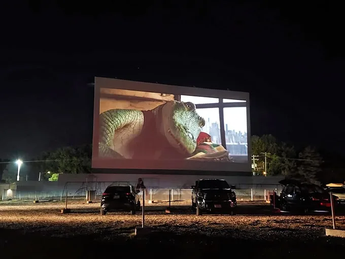 Twilight magic at its finest—cars gathered under a darkening sky as comedy and tragedy masks illuminate the massive screen at Skyview Drive-In.