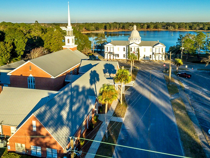 The perfect postcard moment: historic buildings surrounding Lake DeFuniak, where Victorian charm meets Florida sunshine in a scene straight out of a Hallmark movie.