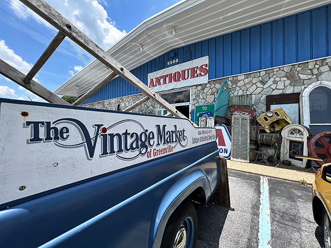 The blue-fronted time machine beckons with its "ANTIQUES" sign, while vintage treasures spill onto the sidewalk like impatient children.