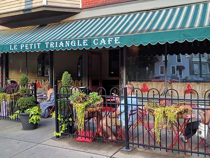 The charming brick facade of Le Petit Triangle Cafe beckons with its distinctive yellow awning and wrought-iron fence—a little slice of Paris on a Cleveland corner.