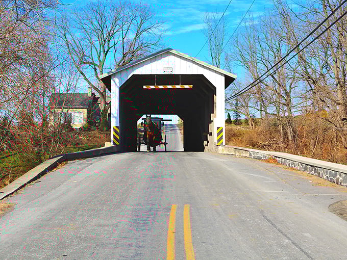 The classic white and red entrance of Eshleman's Mill Covered Bridge stands like a portal to simpler times, complete with an Amish buggy making its way through.