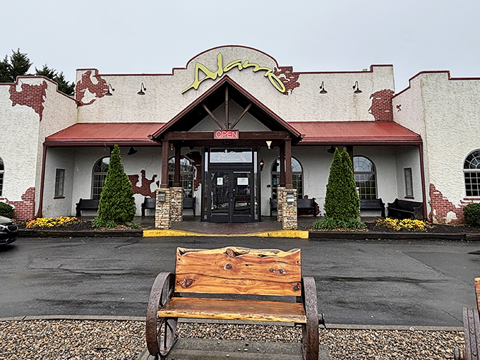 The Alamo Steakhouse's distinctive southwestern facade stands ready to welcome hungry travelers, complete with rustic wagon wheel bench for those inevitable (and worthwhile) wait times.