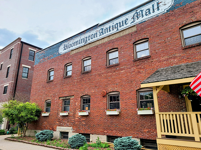 The brick facade of Bloomington Antique Mall stands like a time capsule with its cheerful yellow porch proudly announcing "WE ARE OPEN!" – an invitation to adventure.