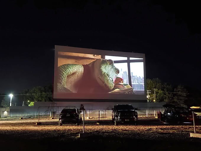 Twilight magic at its finest—cars gathered under a darkening sky as comedy and tragedy masks illuminate the massive screen at Skyview Drive-In.