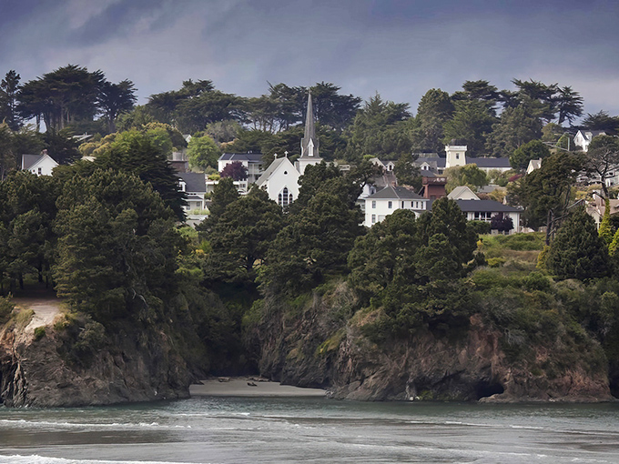 Mendocino perches on dramatic cliffs like nature's balcony, with white buildings peeking through trees above the rugged coastline.